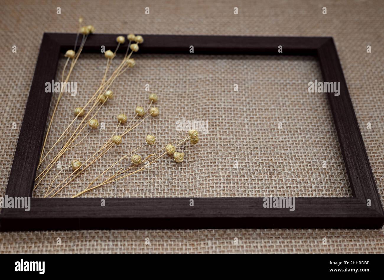 Wooden frame on a background of burlap. Inside the frame is dry flax ...
