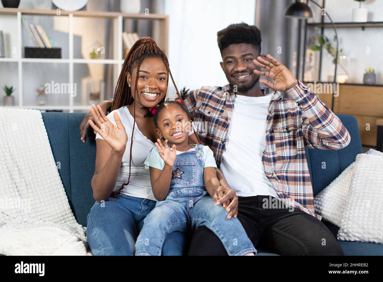 Smiling african parents sitting in hugs with pretty daughter and waving ...