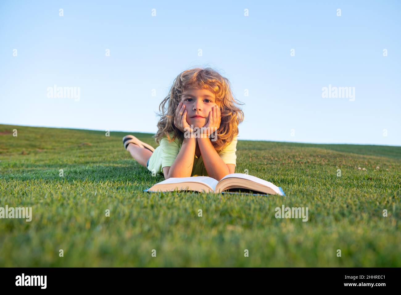 Kid reading book laying on grass on grass and sky background with copy ...