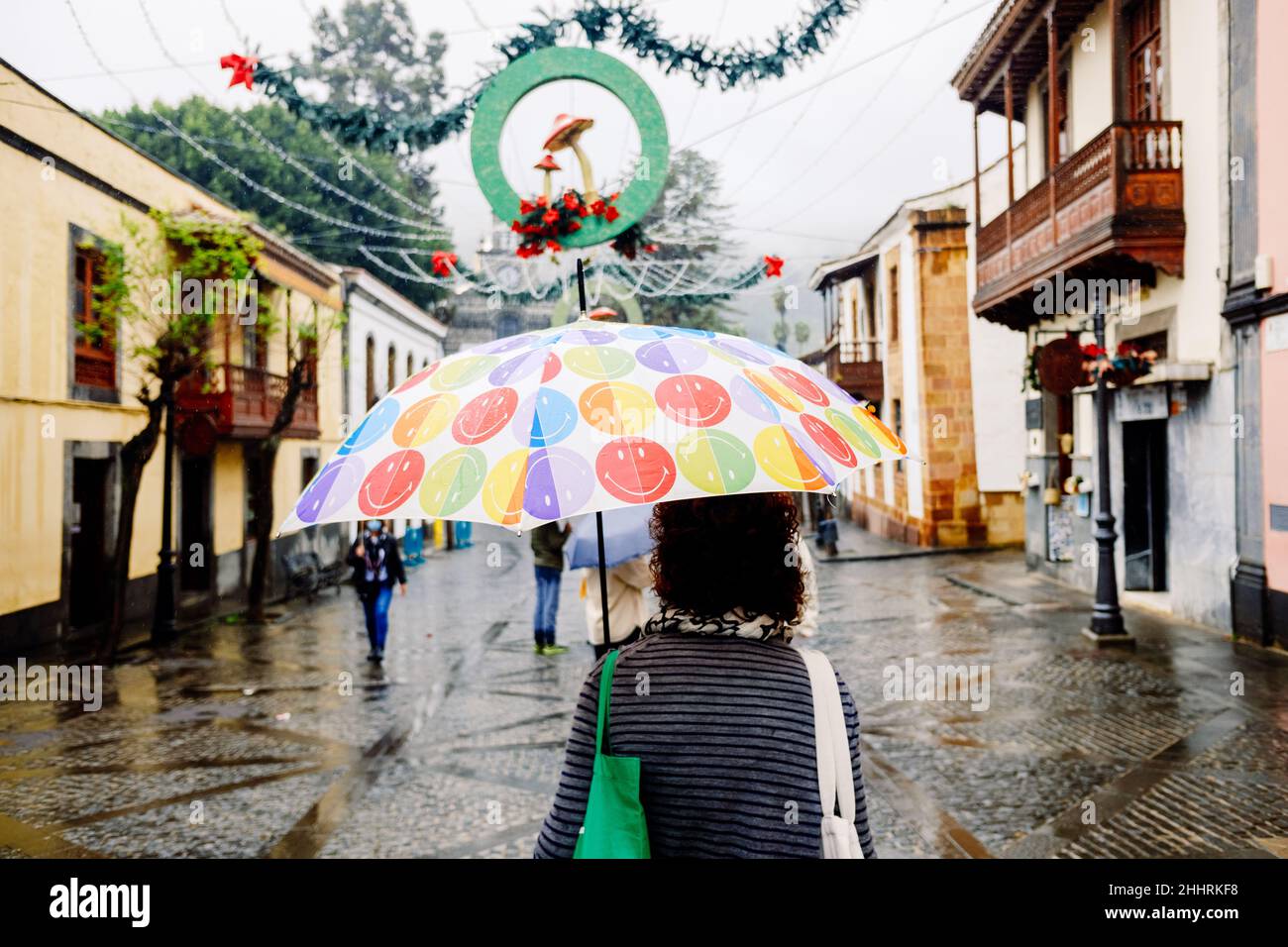 An umbrella with smiley faces protects an unknown woman stroller from ...