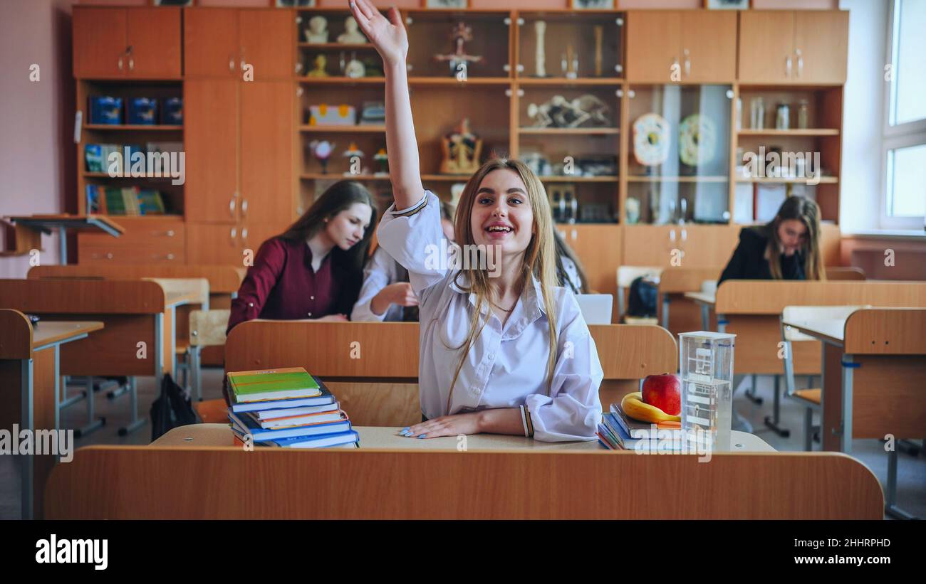 A girl student sitting at a desk raises her hand in the class Stock ...