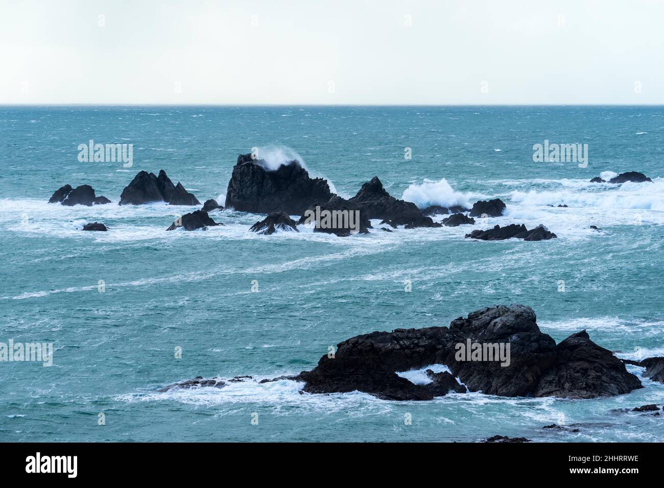 Waves crash into exposed rocks projecting out of the water, off the ...