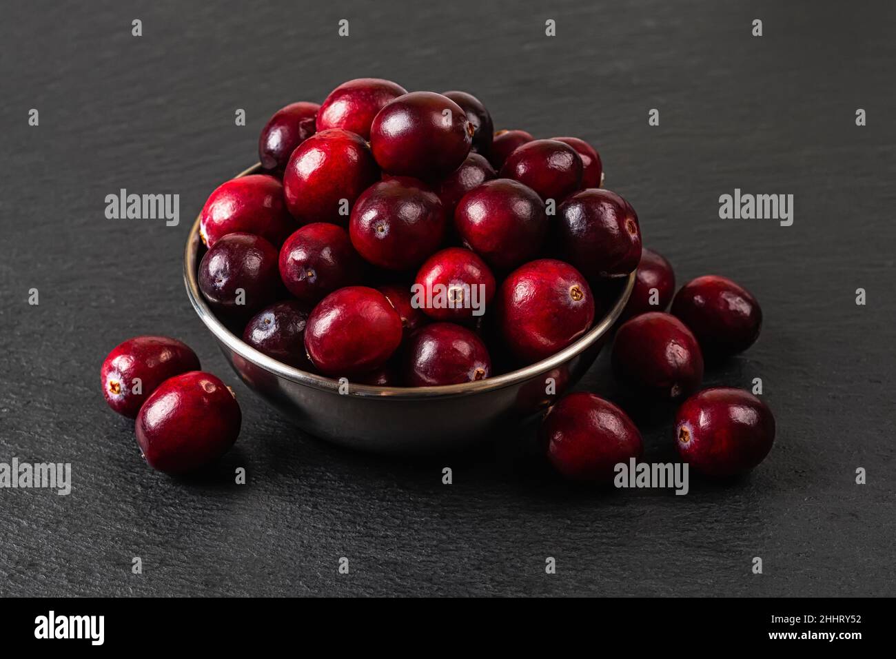 Close-up of red ripe cranberries in a metal bowl on a black slate slab ...