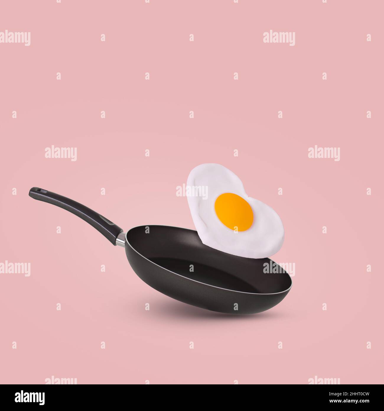 Creative idea with a frying pan and a flying fried egg in heart shape on a bright pink ...