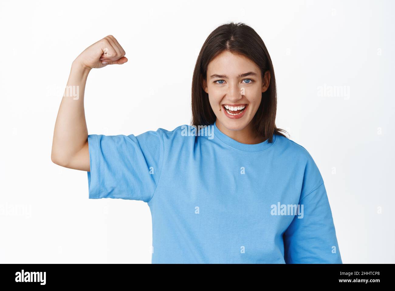 Portrait of cute young woman showing biceps on arms, arm muscles ...