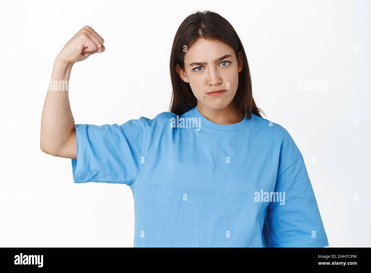 Close up of attractive young girl acting tough, flexing biceps, showing muscles on raised arm ...