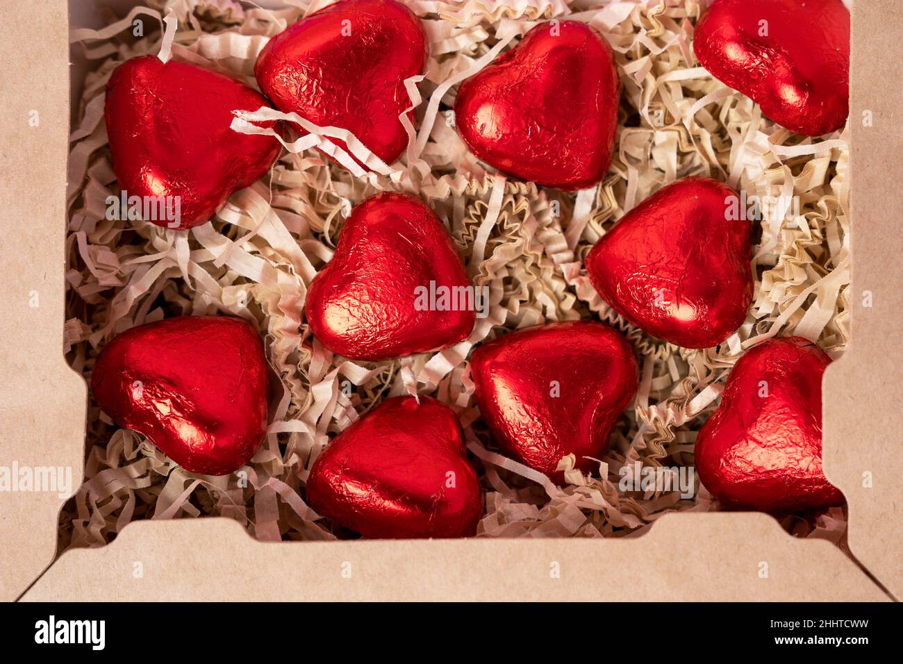 A group of heart-shaped chocolates wrapped in red foil, lying in a gift ...