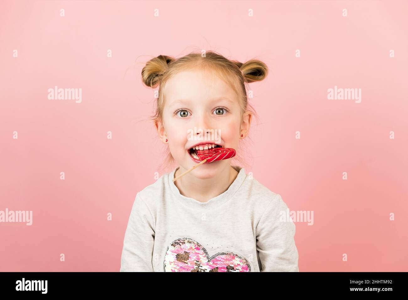 Funny little blonde girl smiling and playing with red heart shape ...