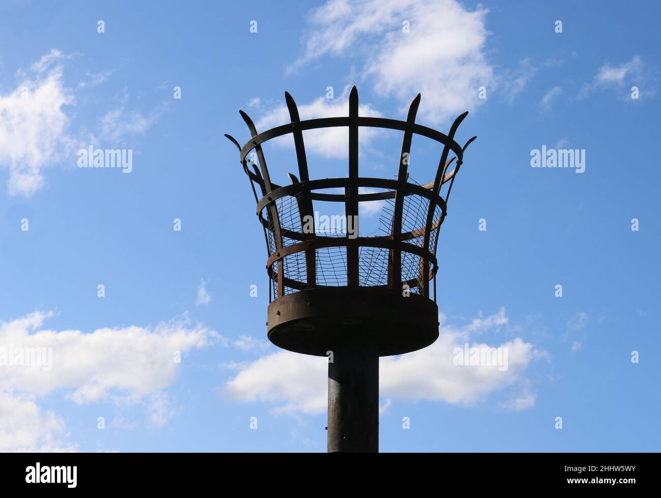 Metal basket fire beacon with wire mesh insert on a pole with a ...