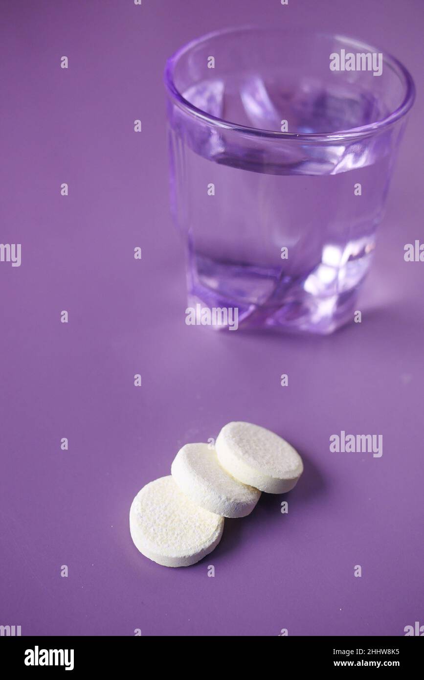 Effervescent soluble tablet pills and glass of water on purple ...