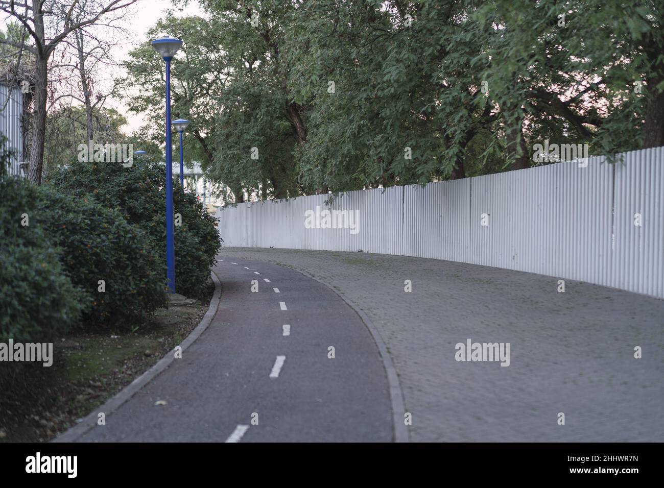 An empty, curved, asphalt bike lane and road lined with high white ...