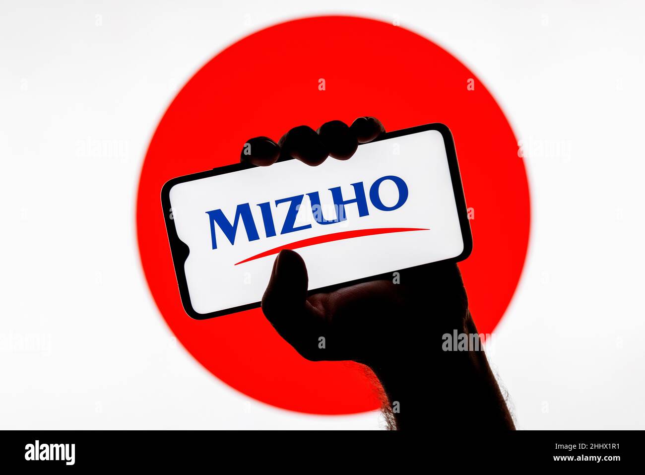 Smartphone with Mizuho Financial Group logo on screen in clenched hand ...