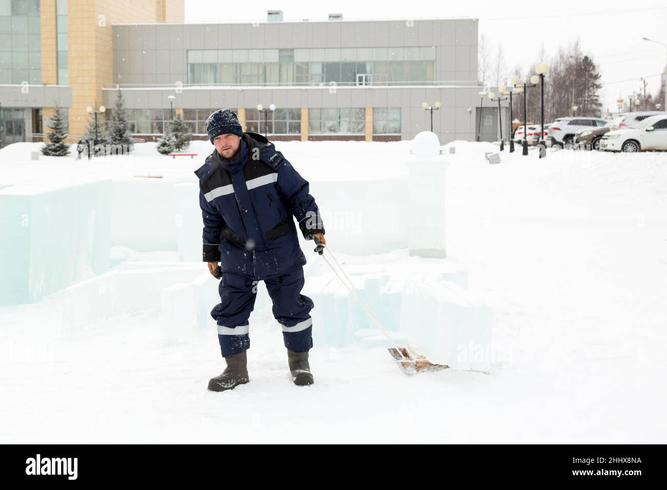 A man in a blue jacket and a black knitted hat is carrying ice panels ...