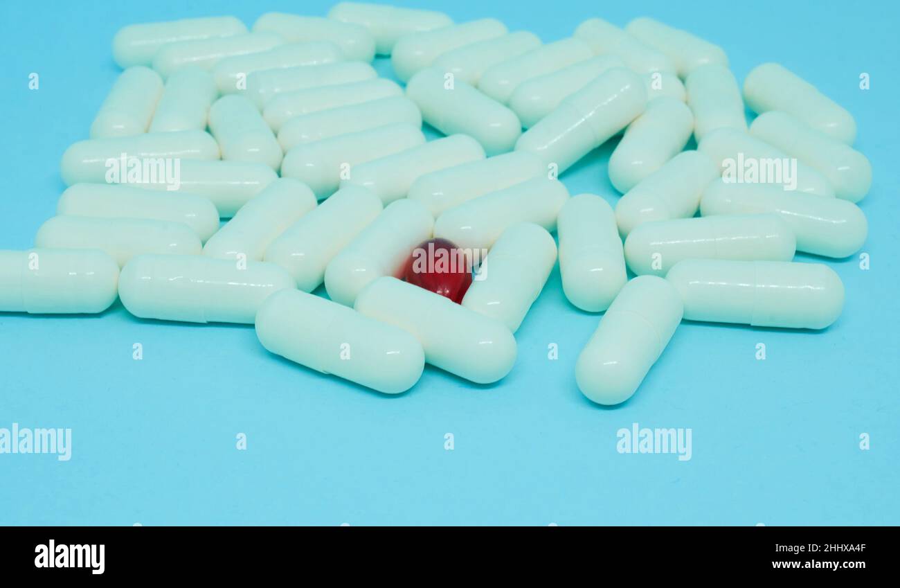 Many white capsules and one dark red capsule are scattered on a blue ...