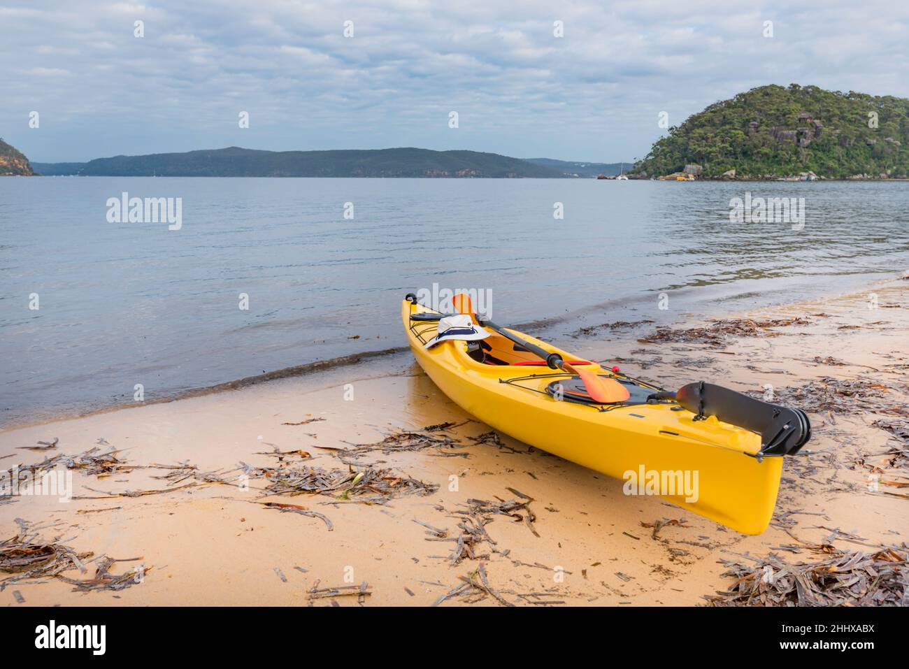 An empty sea kayak with paddle and a wide-brimmed hat sits on the ...