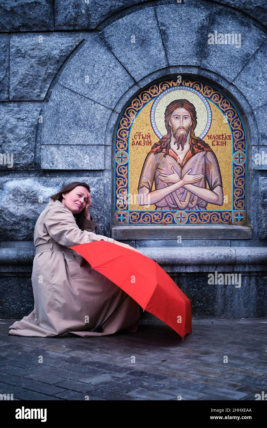 Crying woman with a umbrella at the Christian icon of Jesus Christ ...
