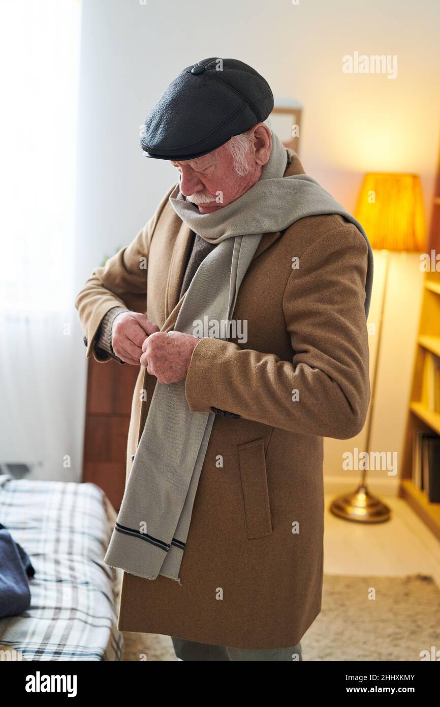 Senior man buttoning elegant coat while standing in living-room of his ...