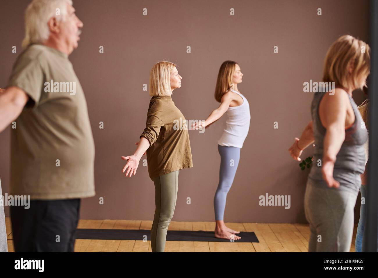 Senior people repeating physical exercise after young female fitness ...