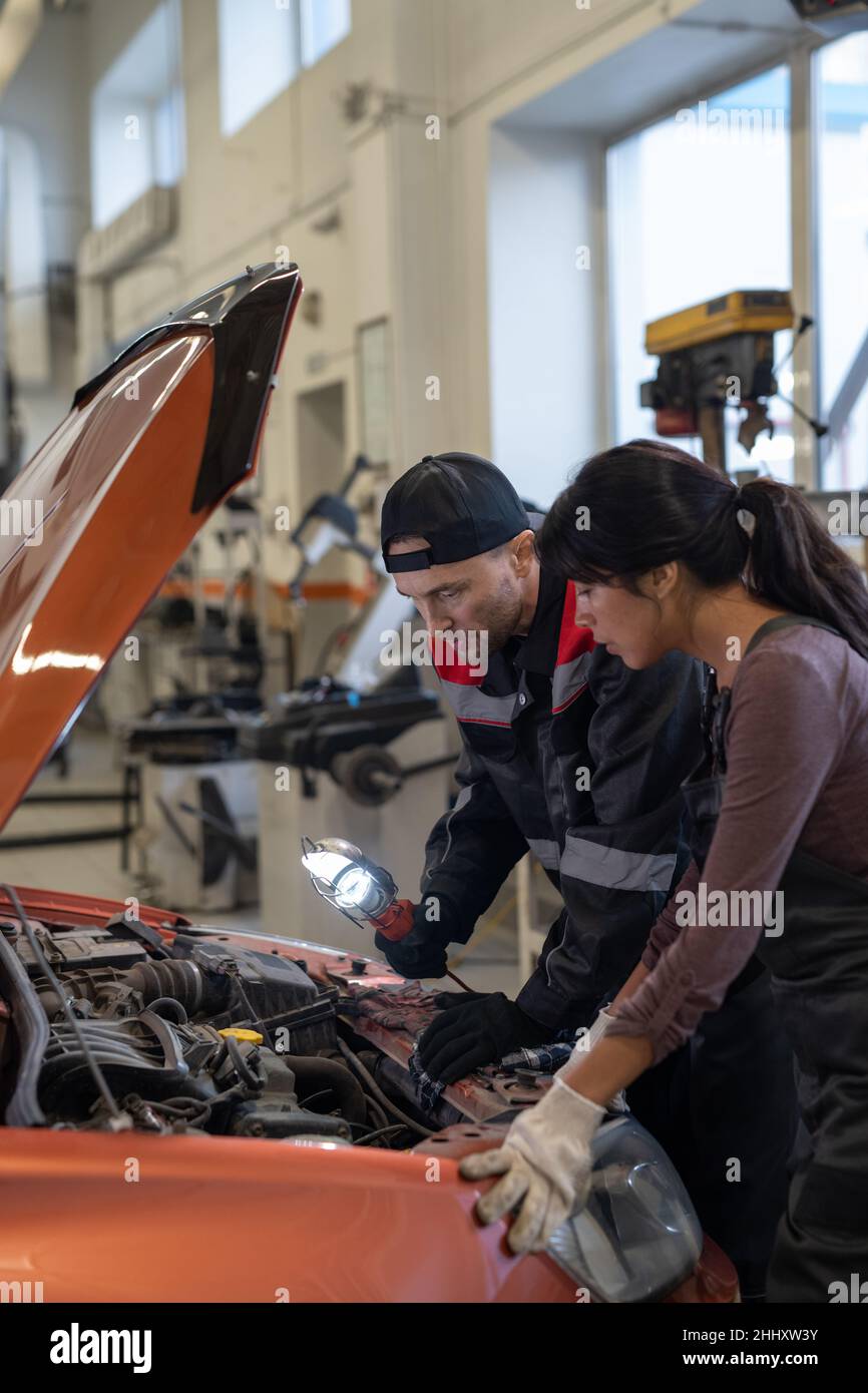 Two young intercultural mechanics in workwear bending over diesel ...