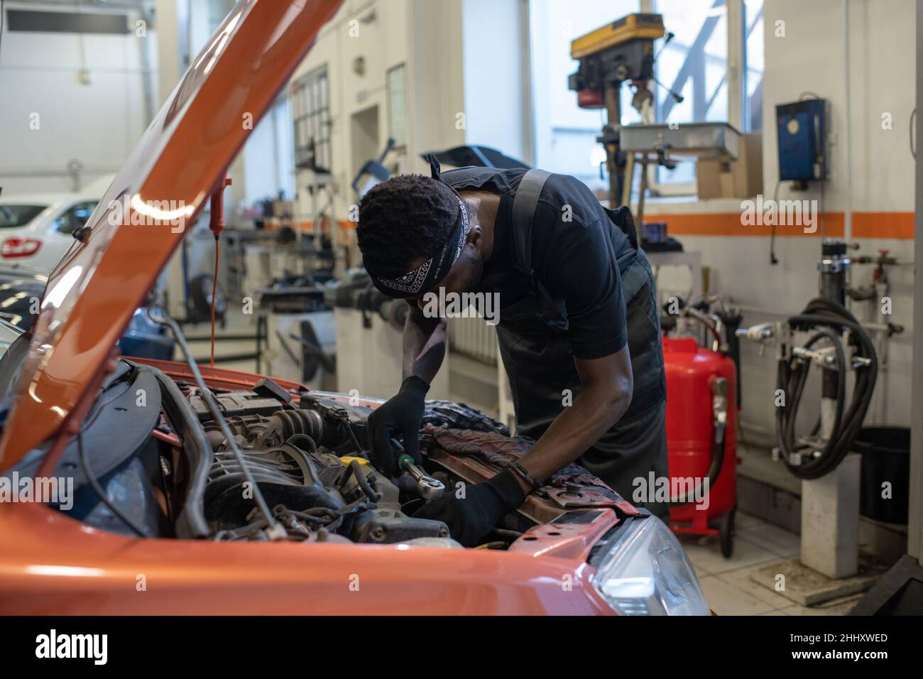 Young black man with handtool checking car engine while bending over ...