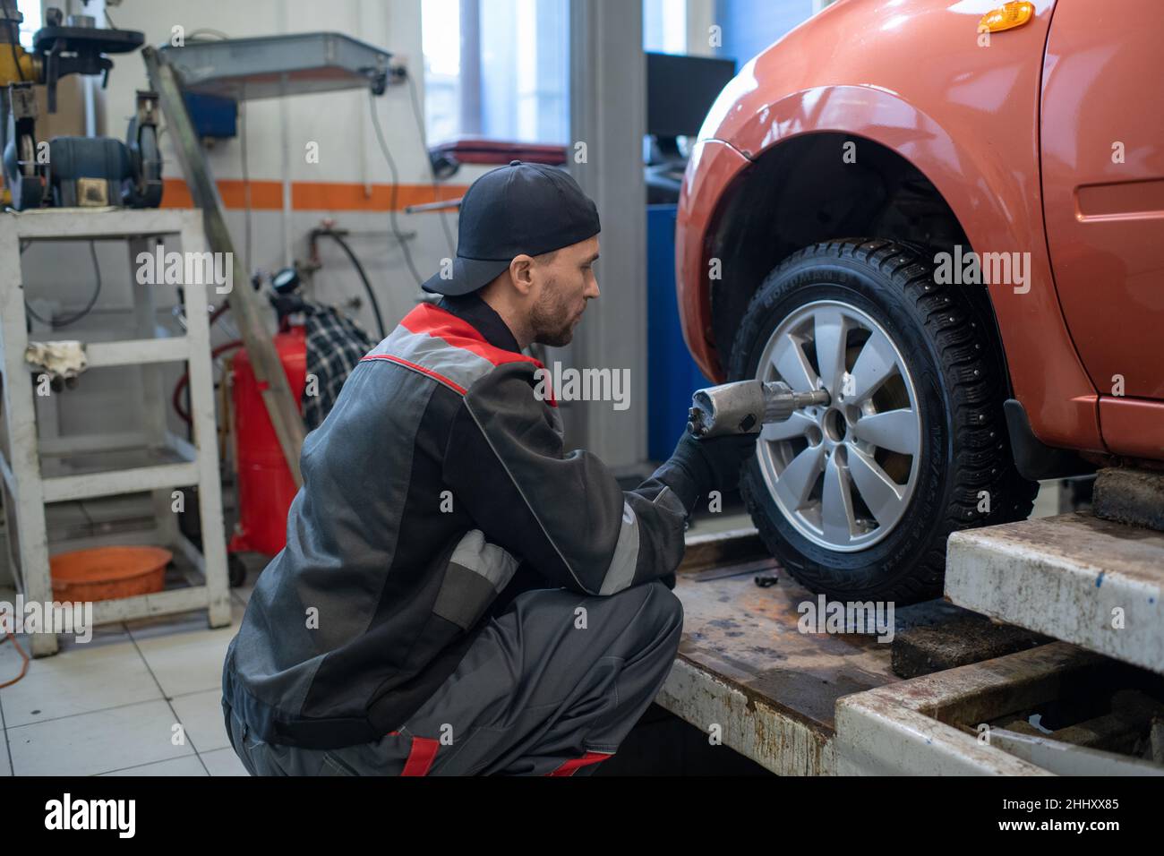 Young repairman in workwear using electric handtool while sitting on ...