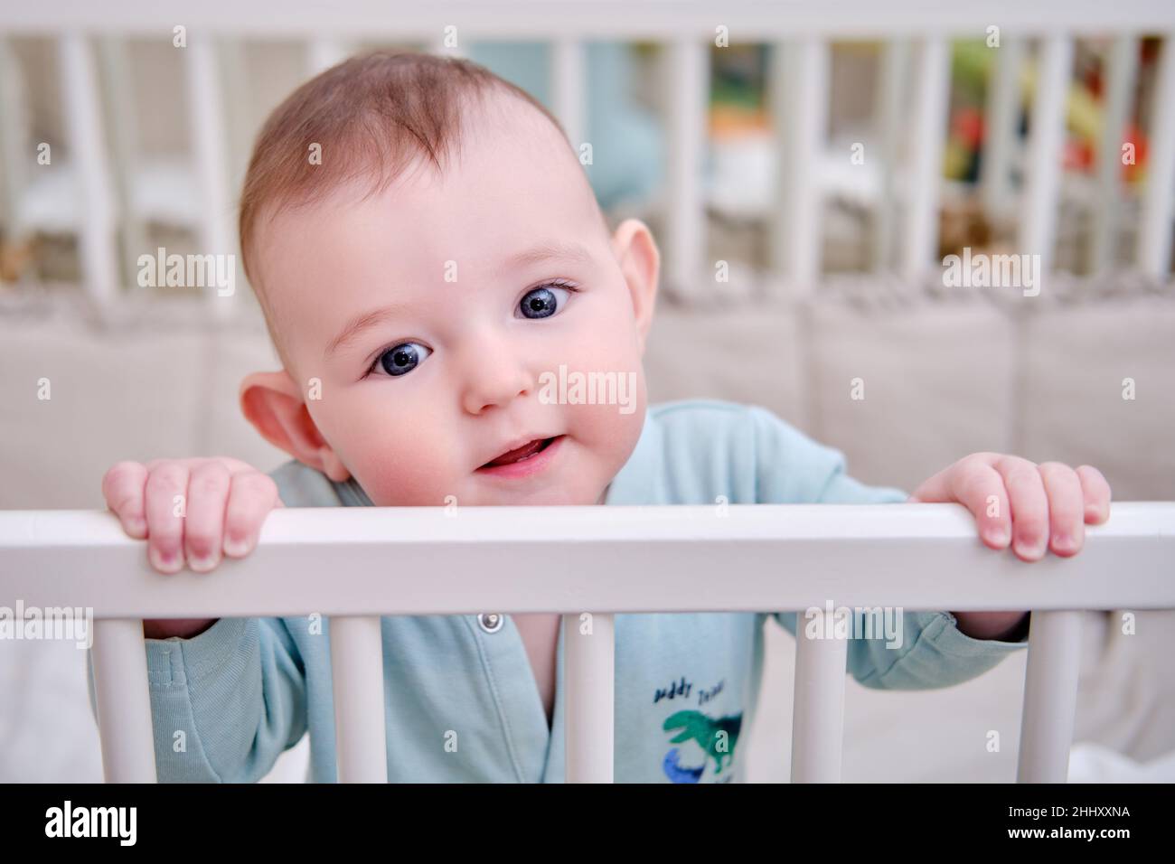 A happy baby is standing in a crib, holding the handrails and smiling ...