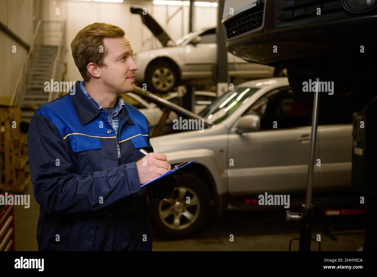 Concentrated young Caucasian technician engineer, auto mechanic writing ...