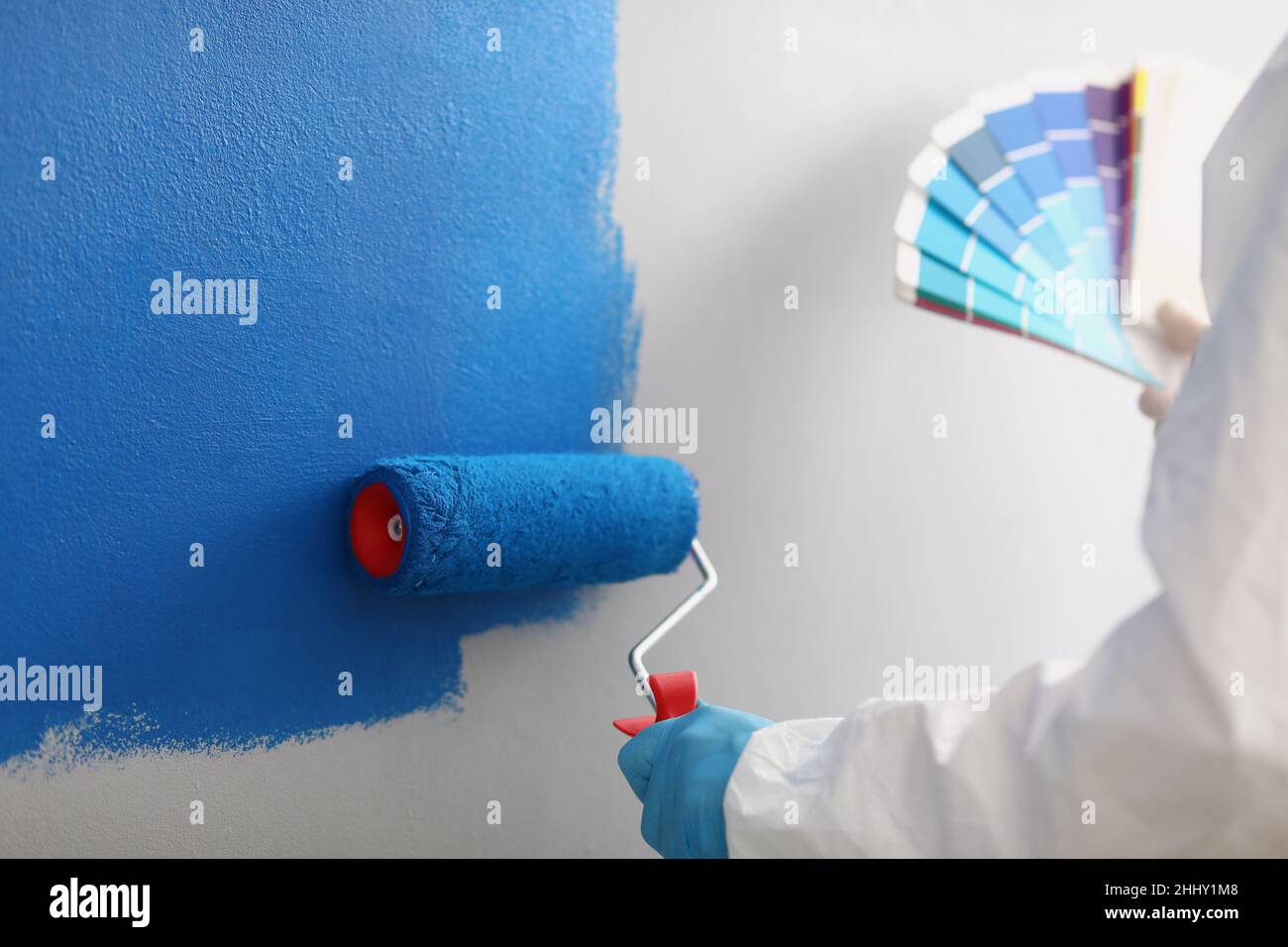 Painter with brush tool covered in blue colour painting wall, worker on ...