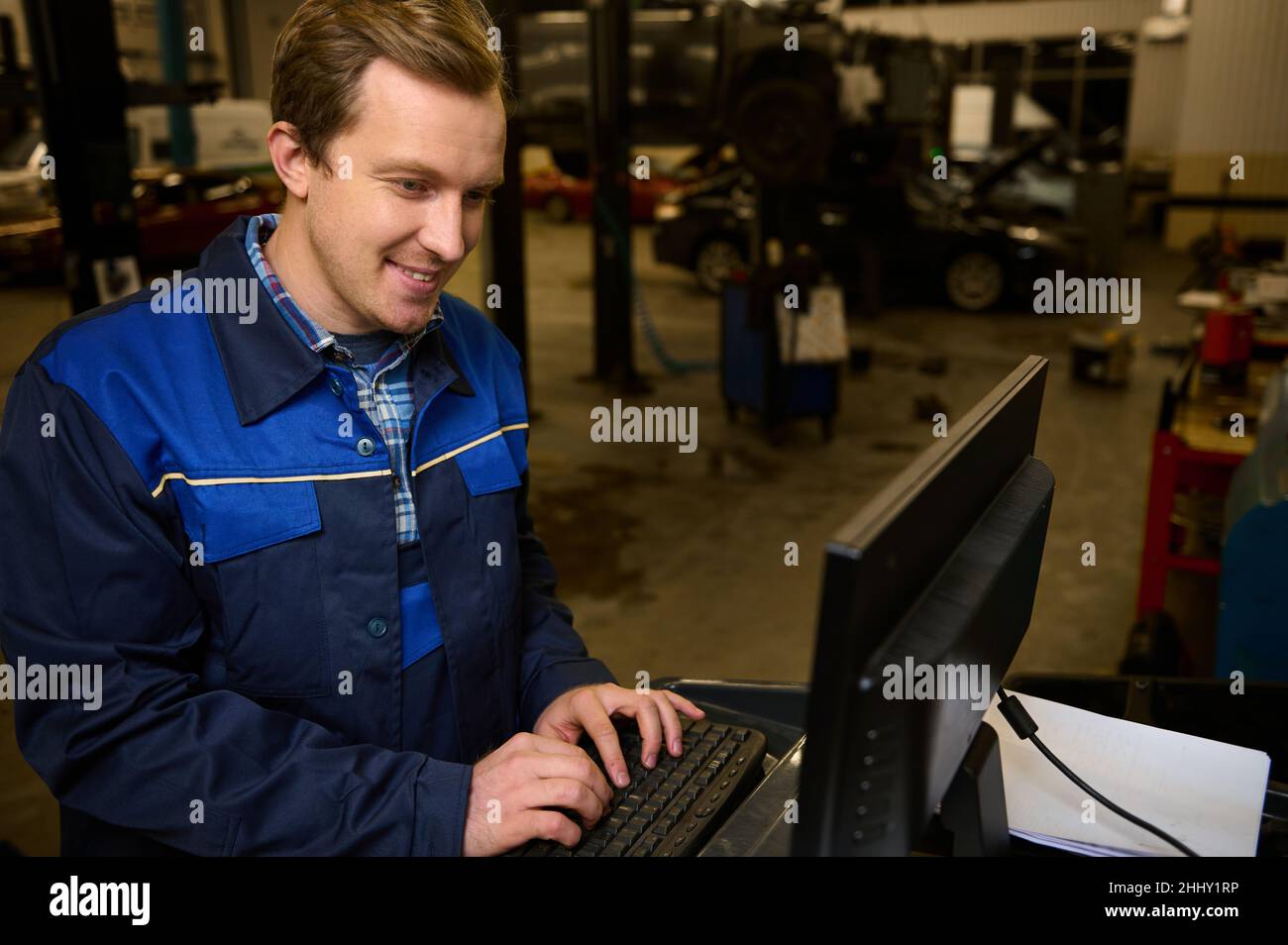 A technician, car engineer, garage mechanic typing on keyboard, making ...