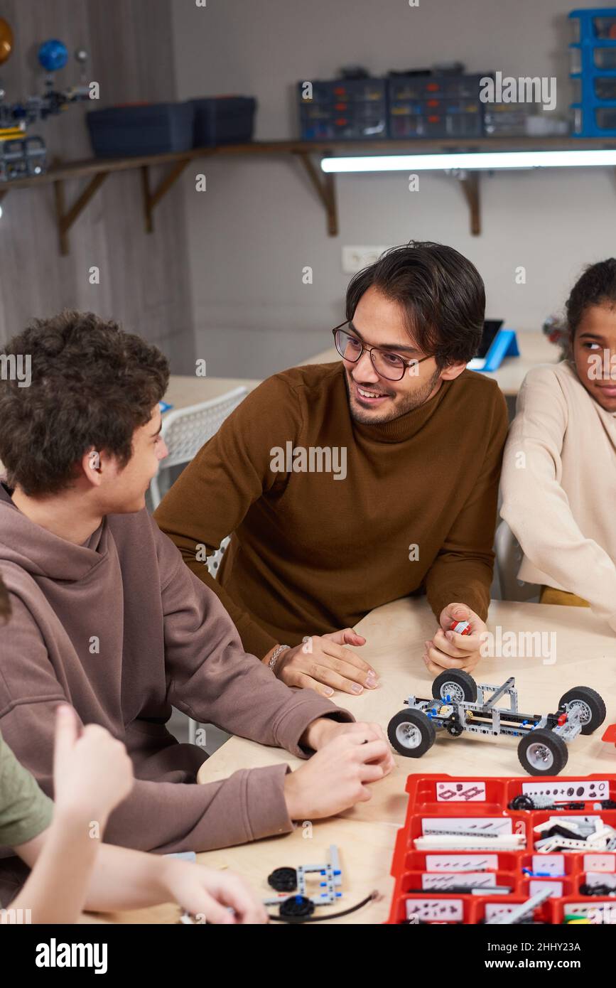 Happy young man helping children to construct an artificial model at ...
