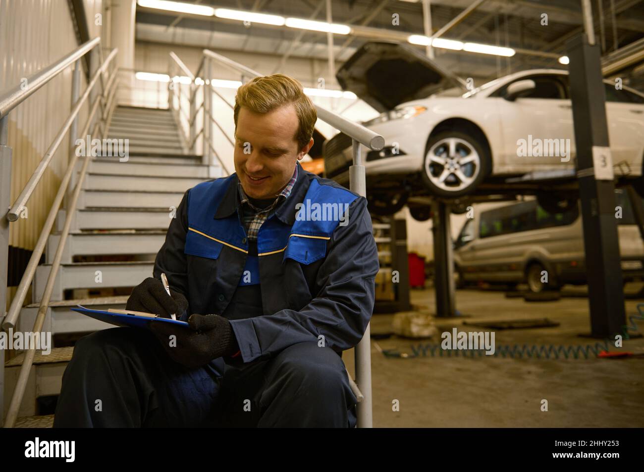 Young Caucasian auto mechanic sitting on stairs in the repair shop and ...