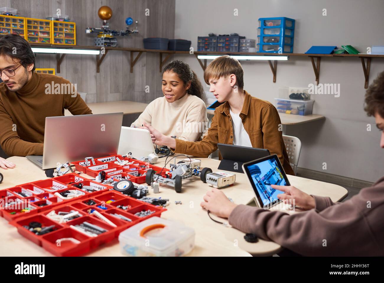 Teenagers using laptop to connect their robots while they sitting at ...