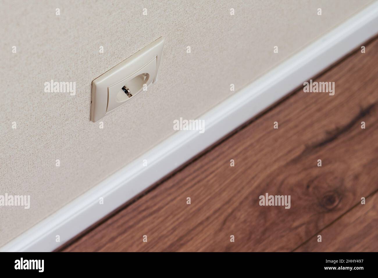 Electrical outlet on beige home wall with wallpaper, white baseboard ...