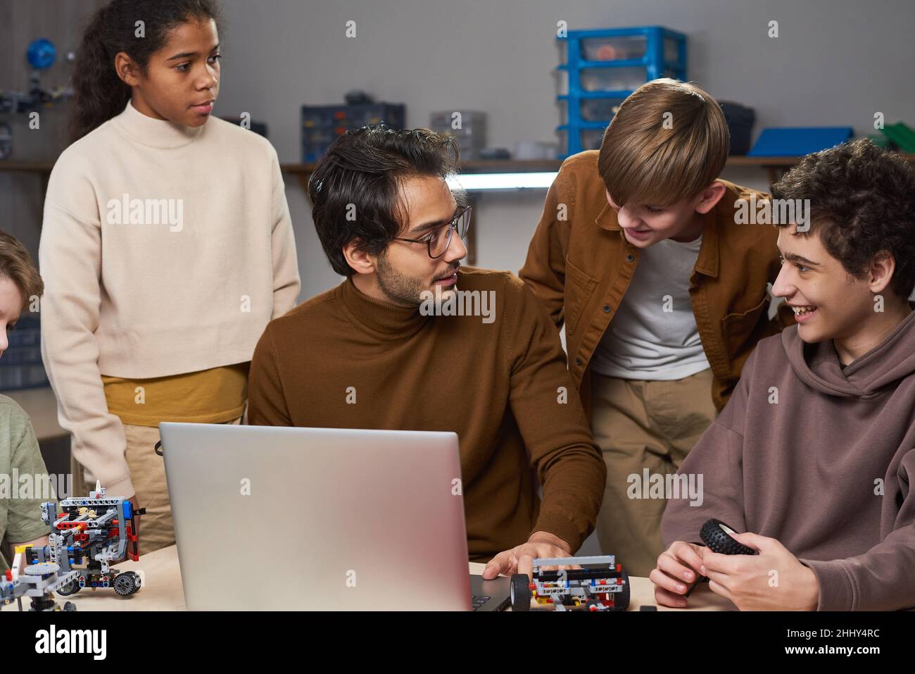 Young teacher teaching robotics lesson for his students at the table ...