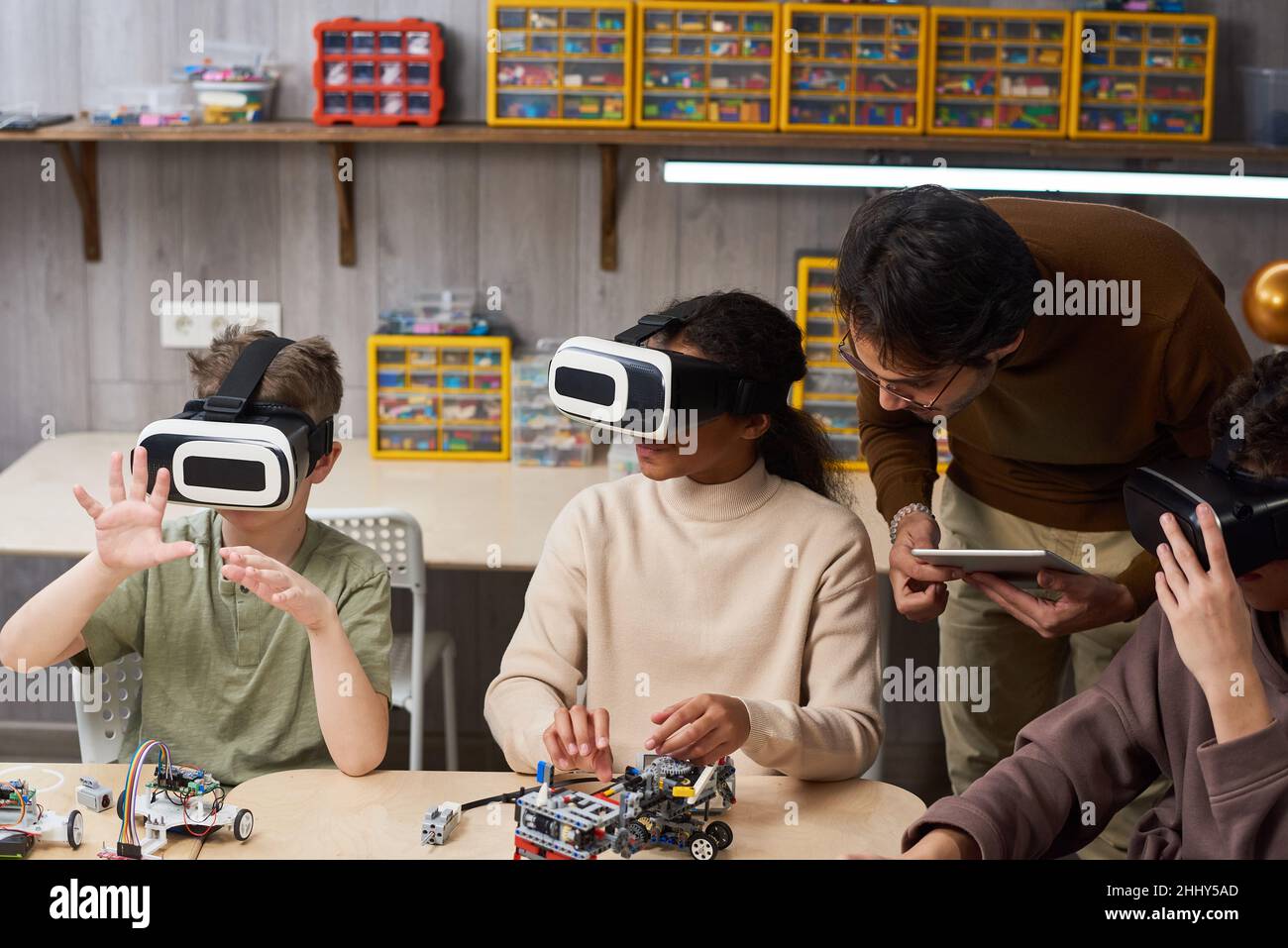 Group of children sitting at the table and projecting robots in vr ...