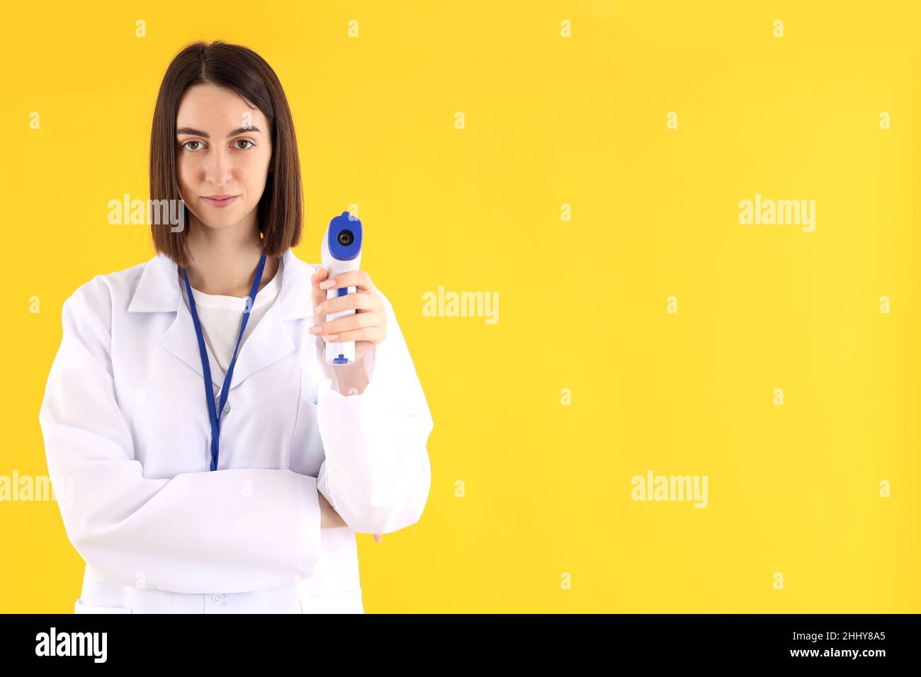 Female trainee doctor with thermometer gun on yellow background Stock ...