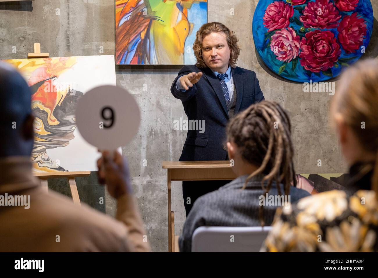 Mature man in suit pointing at man with tablet, people buying paintings ...