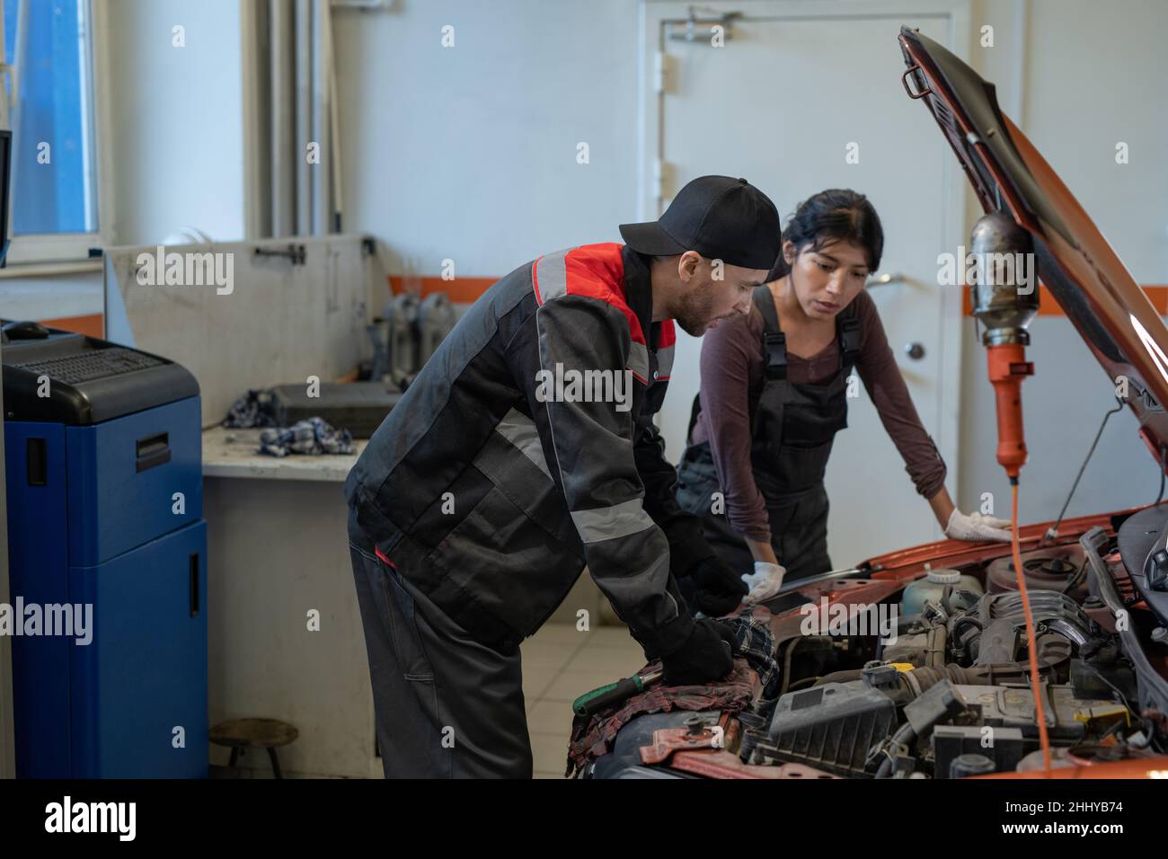 Two colleagues in workwear checking engine of car and consulting about ...
