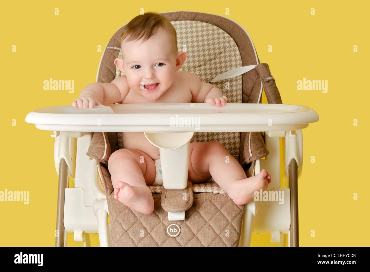Happy baby sits on a high chair for feeding children, studio yellow ...