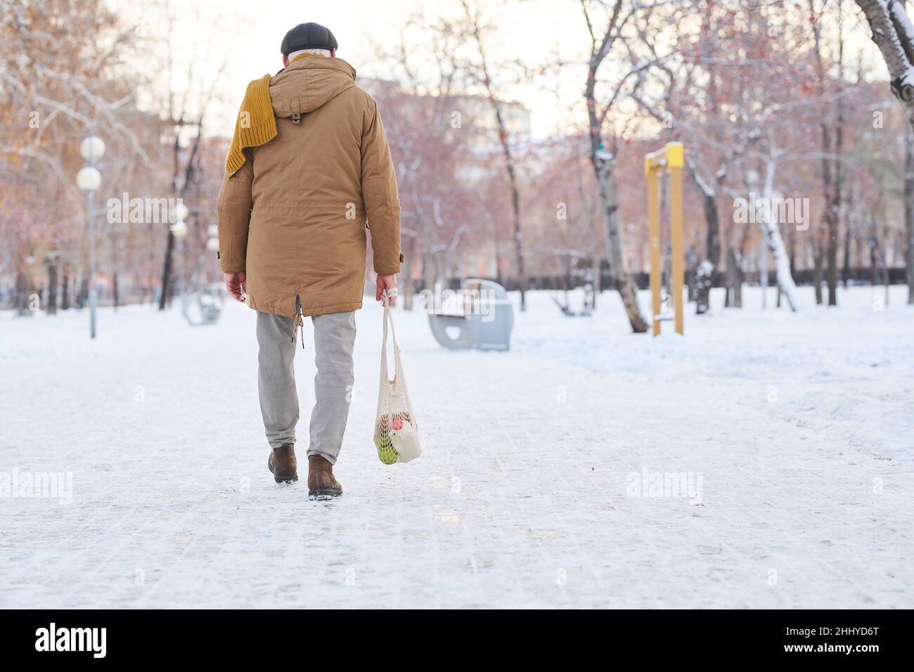 Rear view of old man in warm casualwear moving down road in park while ...