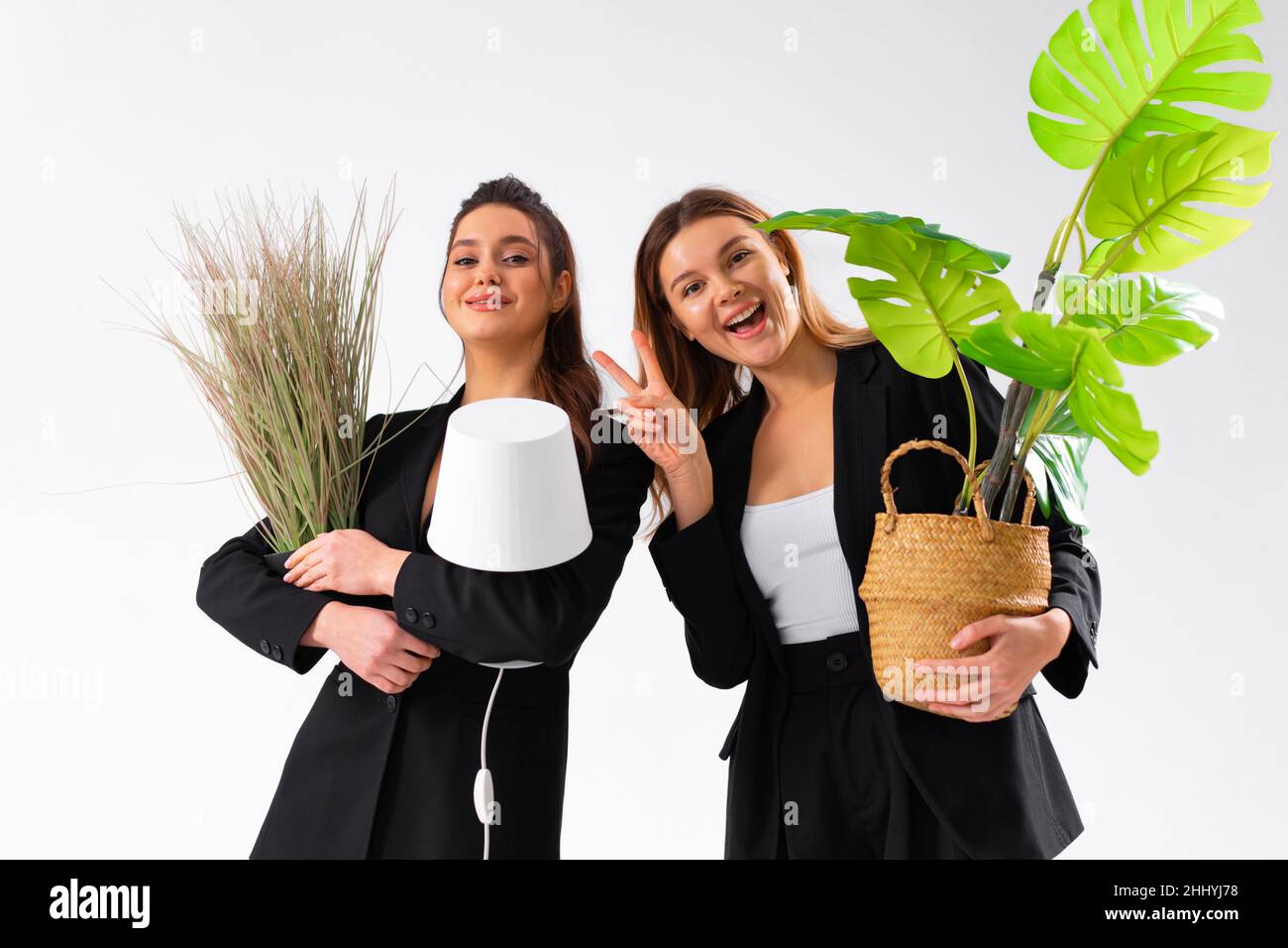 Two business woman dressed black suit smile holding houseplant and lamp ...
