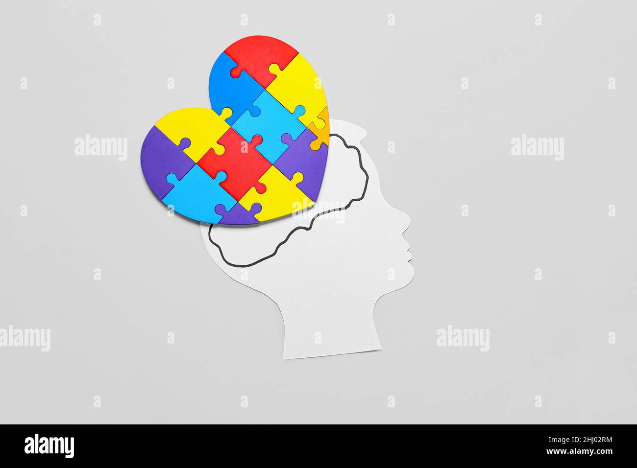 Paper human head with colorful puzzle pieces in shape of heart on light ...