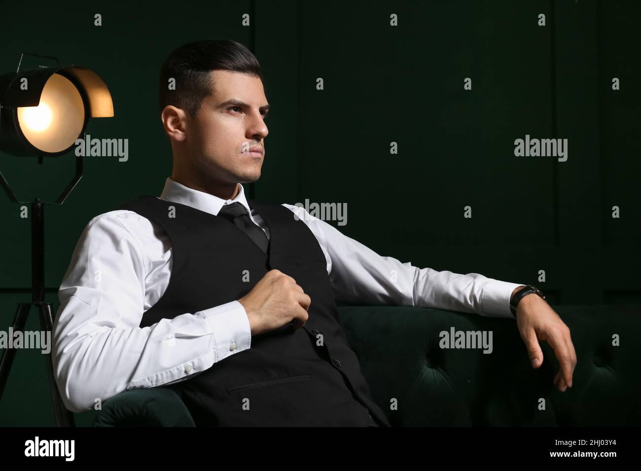 Fashionable gentleman sitting on sofa in dark room Stock Photo - Alamy