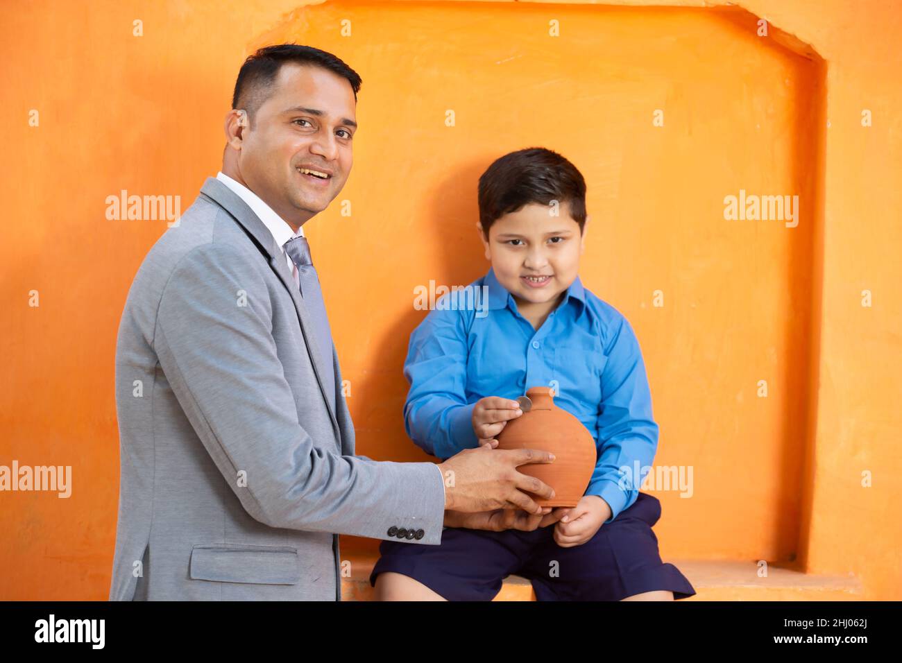 Portrait of Indian man with little kid putting coin into clay money box ...