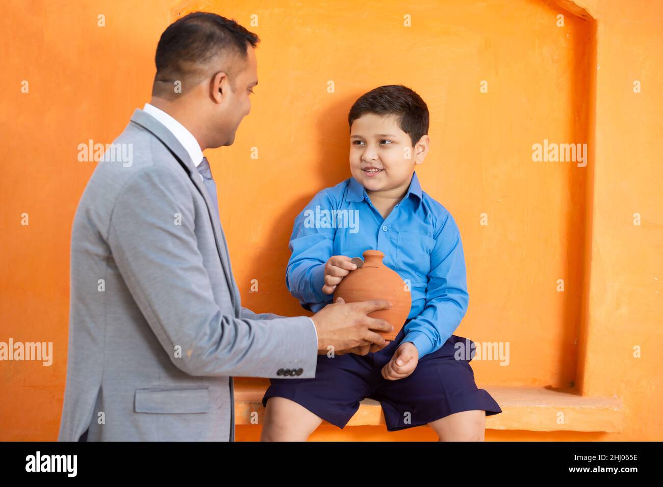 indian man with little kid putting coin into clay money box.male bank ...