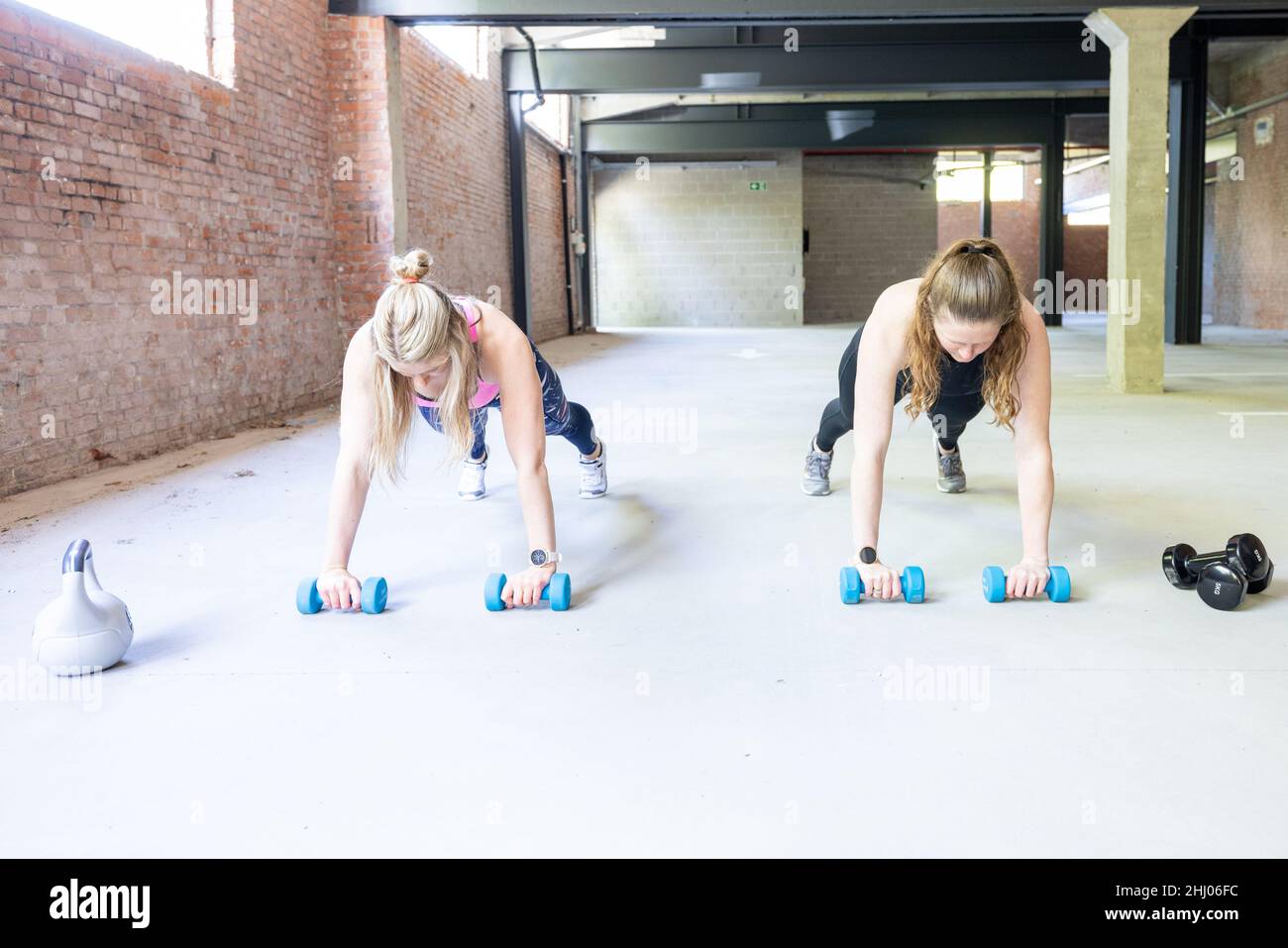 Two young attractive women doing push ups inside with barbells. Fitness ...