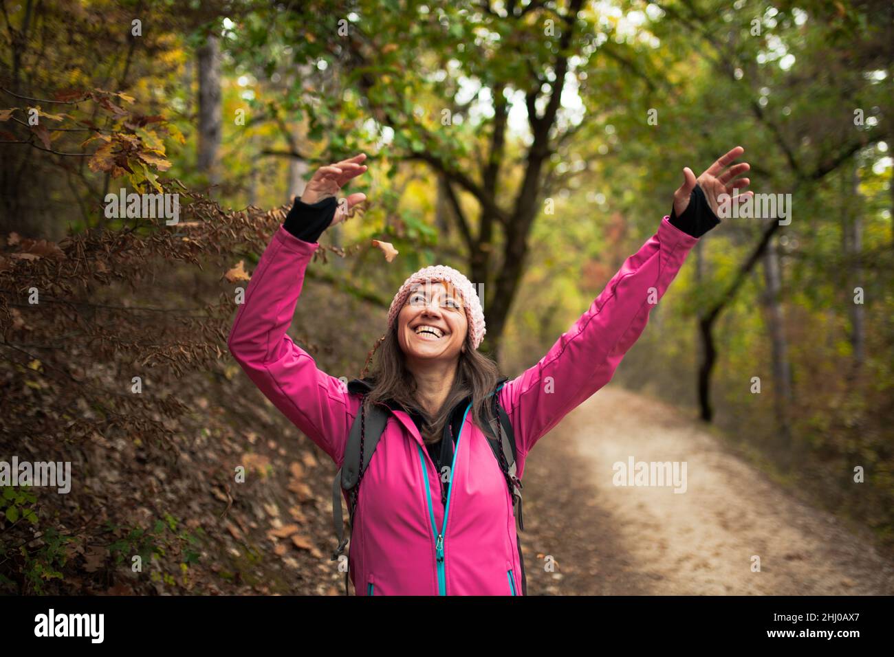 Hiking girl in pink on a trail in the forest. Hands up enjoying the ...