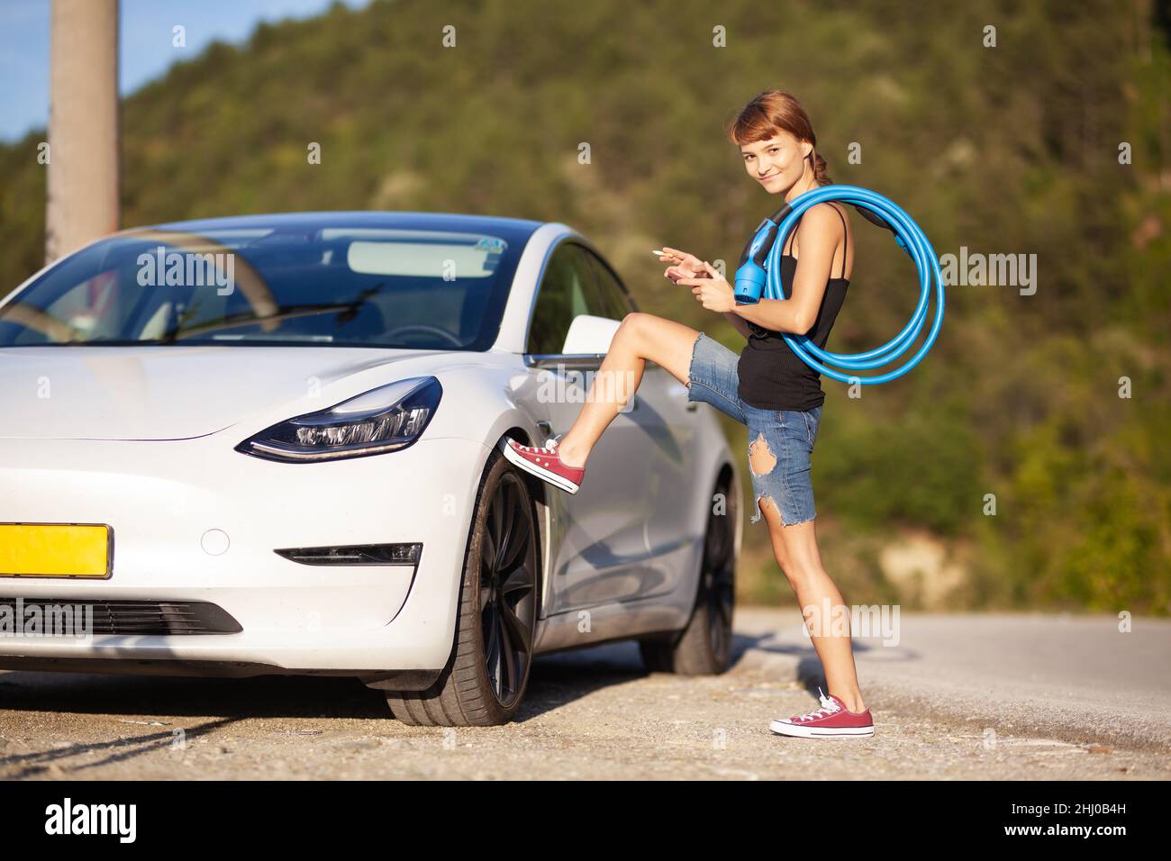 Beautiful young girl next to an electric car. Standing with a blue ...