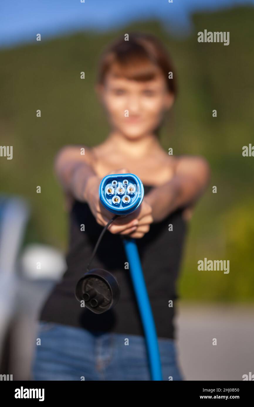 Beautiful young girl next to an electric car. Posing and holding a ...