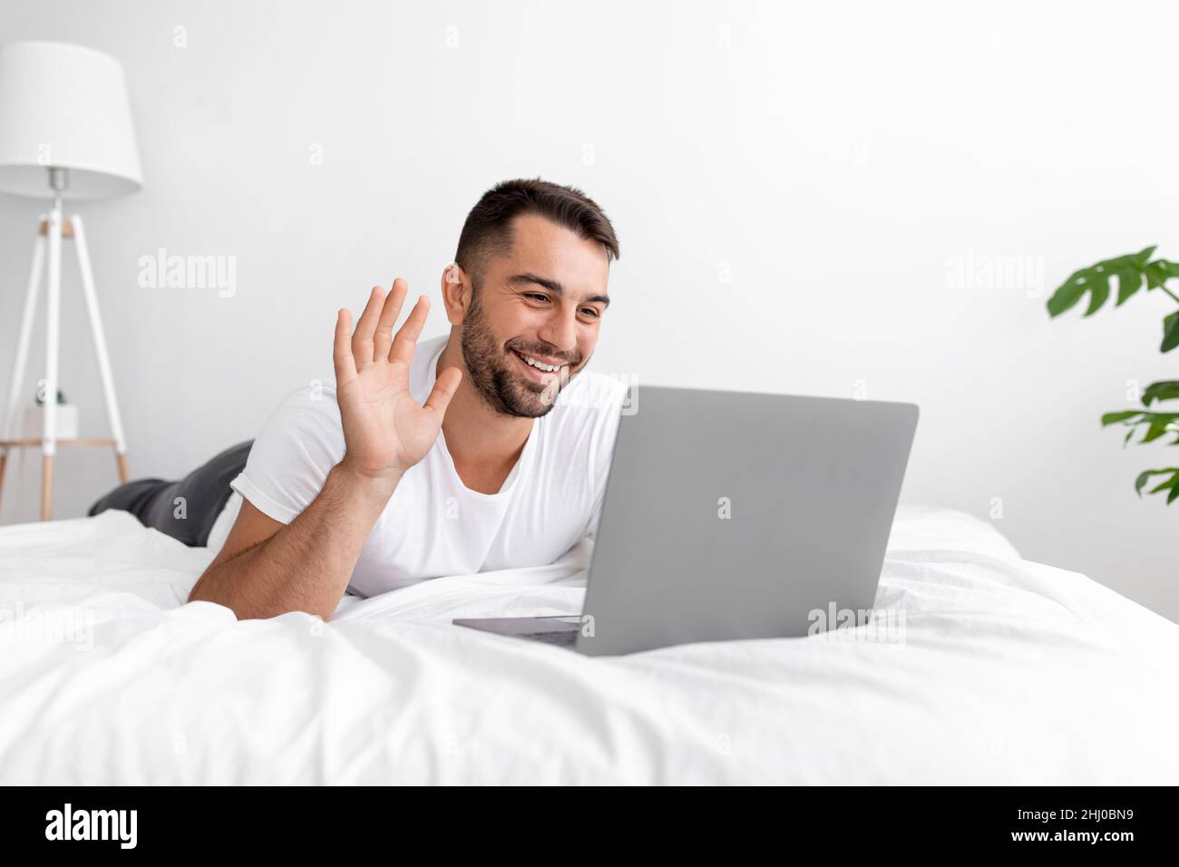 Happy relaxed millennial caucasian muscular guy lies on white bed ...